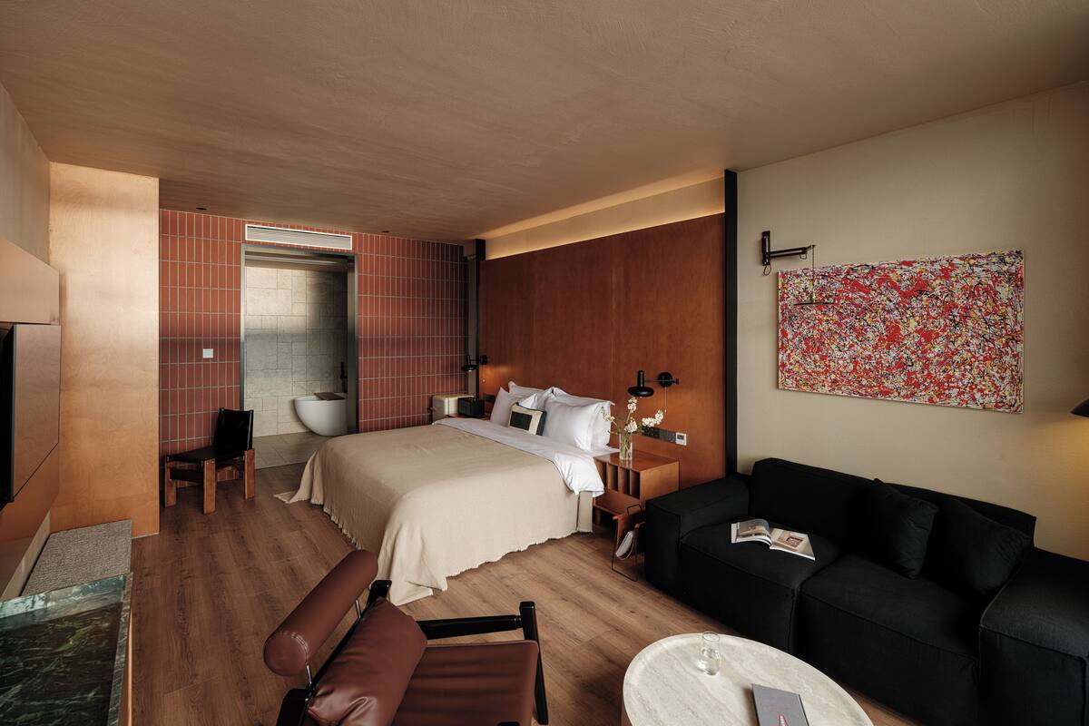 Quarto de hotel moderno com uma cama, um sofá preto, uma mesinha e um banheiro com chuveiro e vaso sanitário.