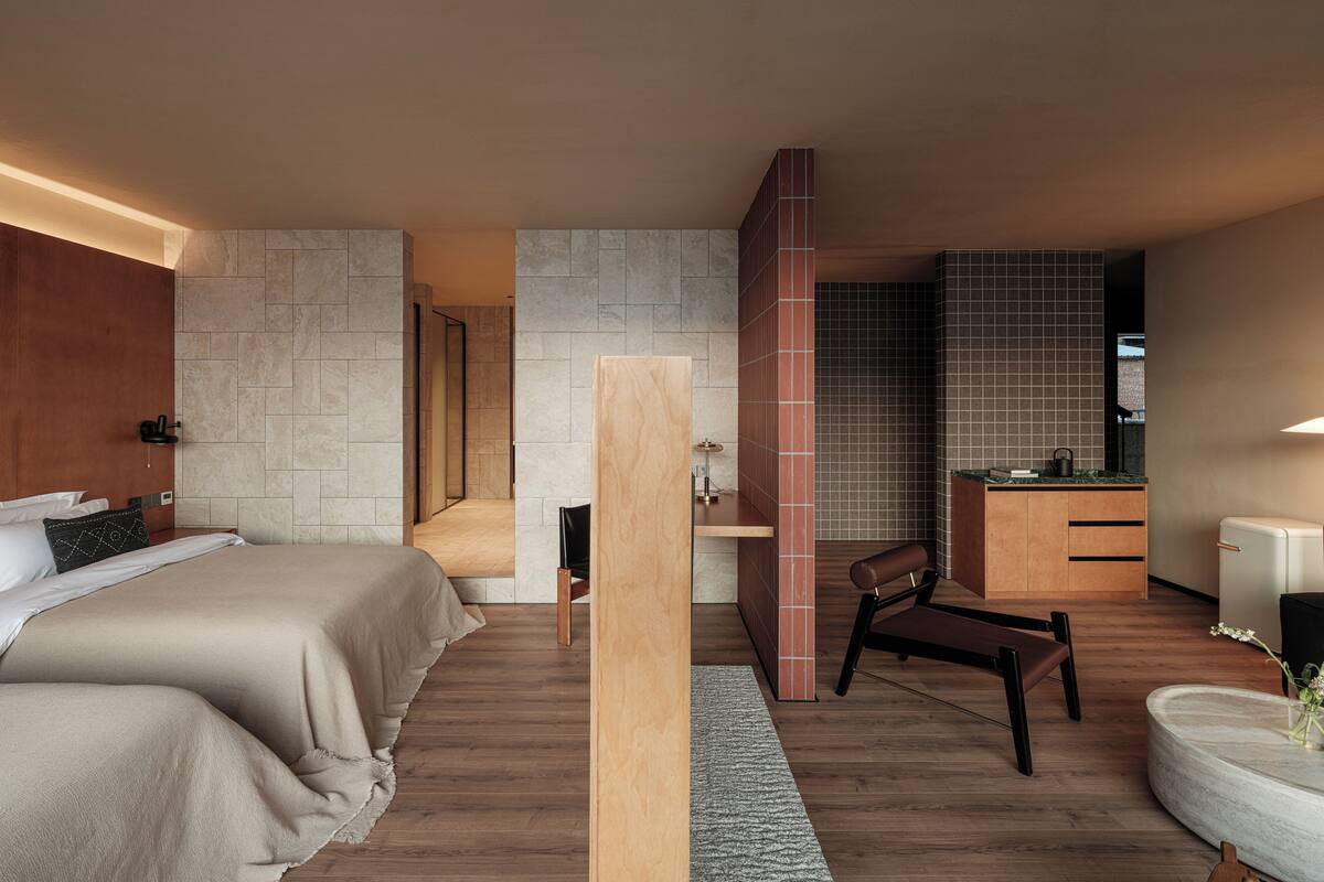 Quarto de hotel moderno com cama, escrivaninha, cadeira e banheiro visível por uma porta aberta.