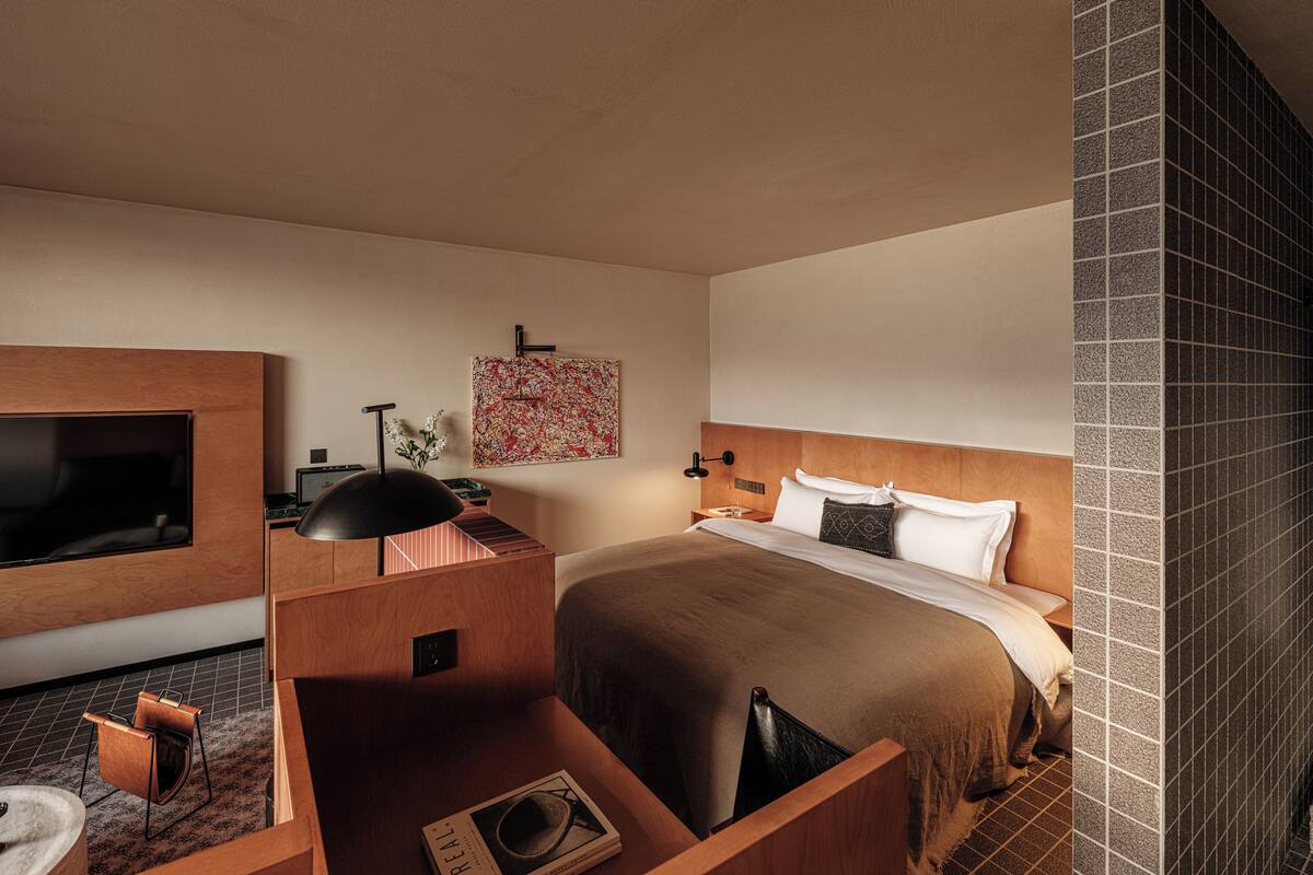 Quarto de hotel com cama grande, televisão, escrivaninha e uma obra de arte moderna na parede.