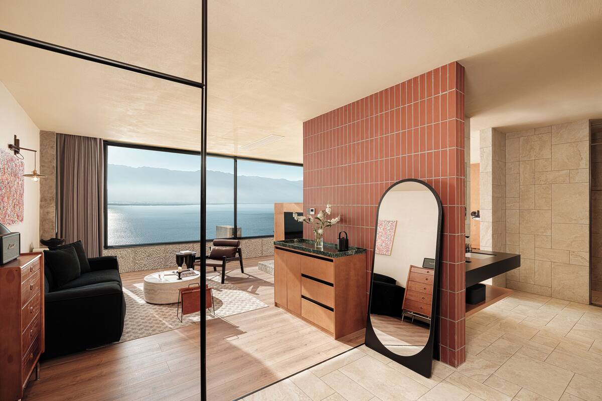 Quarto de hotel moderno com uma grande janela que oferece vista para o mar, um espaço de estar aconchegante, uma mesa de toucador com espelho e piso de madeira.