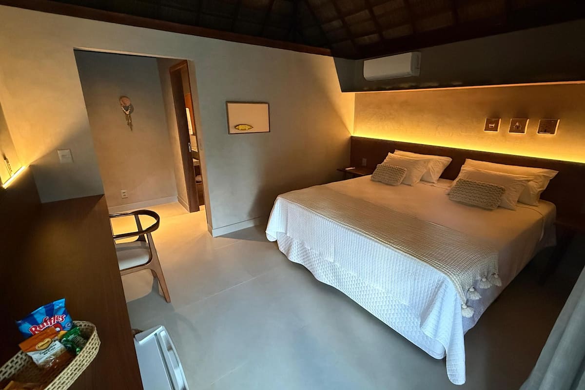 Quarto com uma cama grande, mesas de cabeceira, um criado-mudo, uma cadeira e uma pequena mesa com lanches.