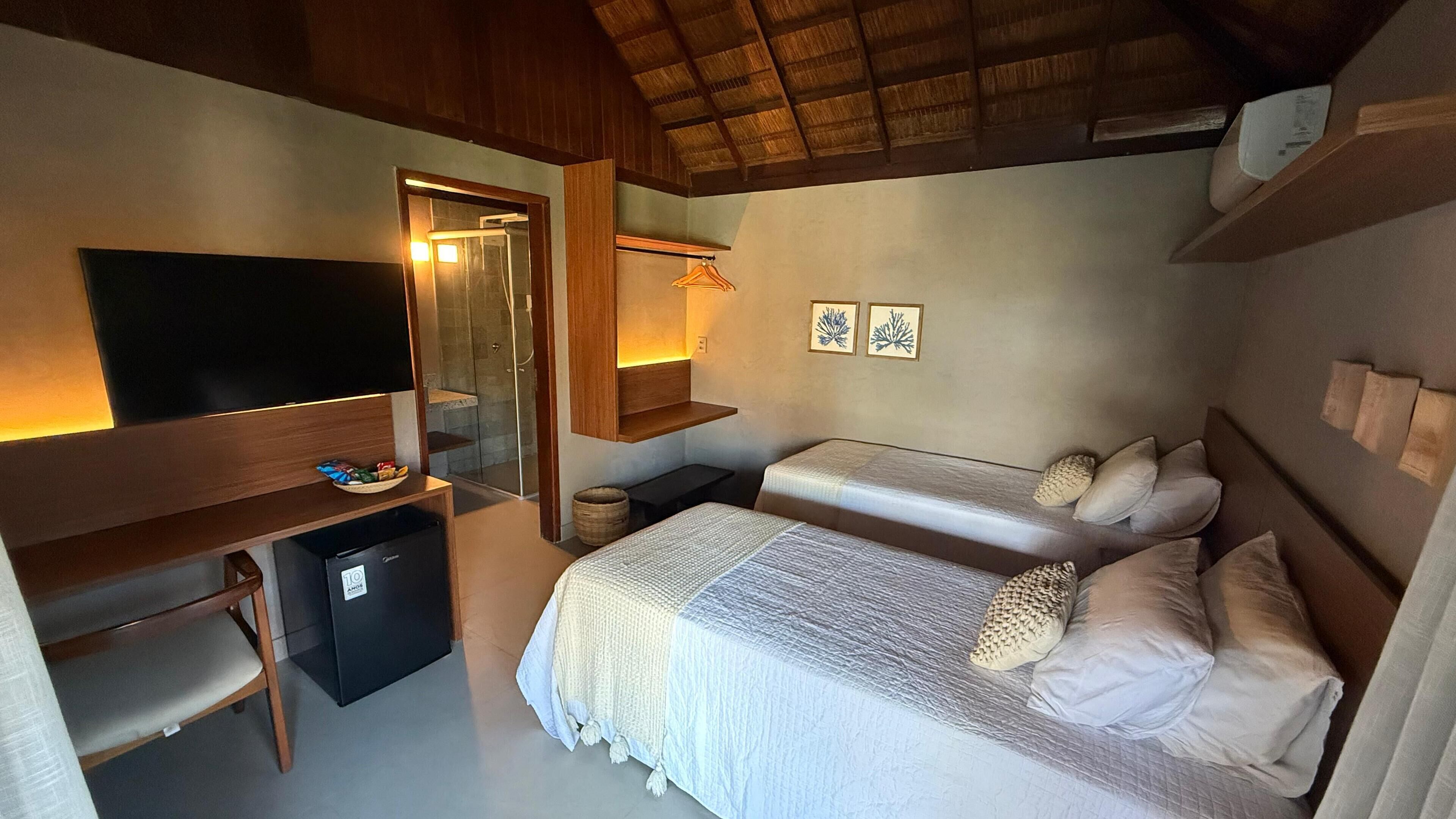 Quarto compacto com uma cama de solteiro, escrivaninha, cadeira, televisão e área de chuveiro.