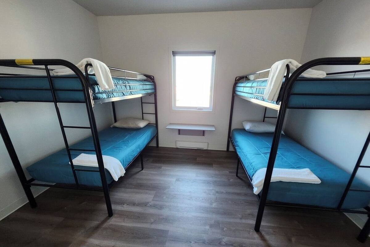 Quarto com duas beliches, uma janela pequena e um banco.