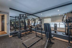 Uma academia com diversos equipamentos de exercício, um espelho e uma esteira.
