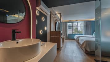 Quarto de hotel moderno com uma pia grande e redonda, um espelho, um guarda-roupa, uma cama e uma janela com vista para edifícios.