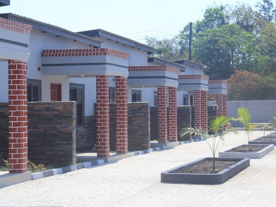 Uma fileira de edifícios modernos com pilares de tijolo e paredes de pedra, um calçada pavimentada e pequenas plantas em vasos.
