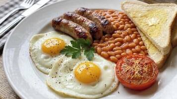 Um prato com ovos, salsichas, feijão, torradas e um tomate.