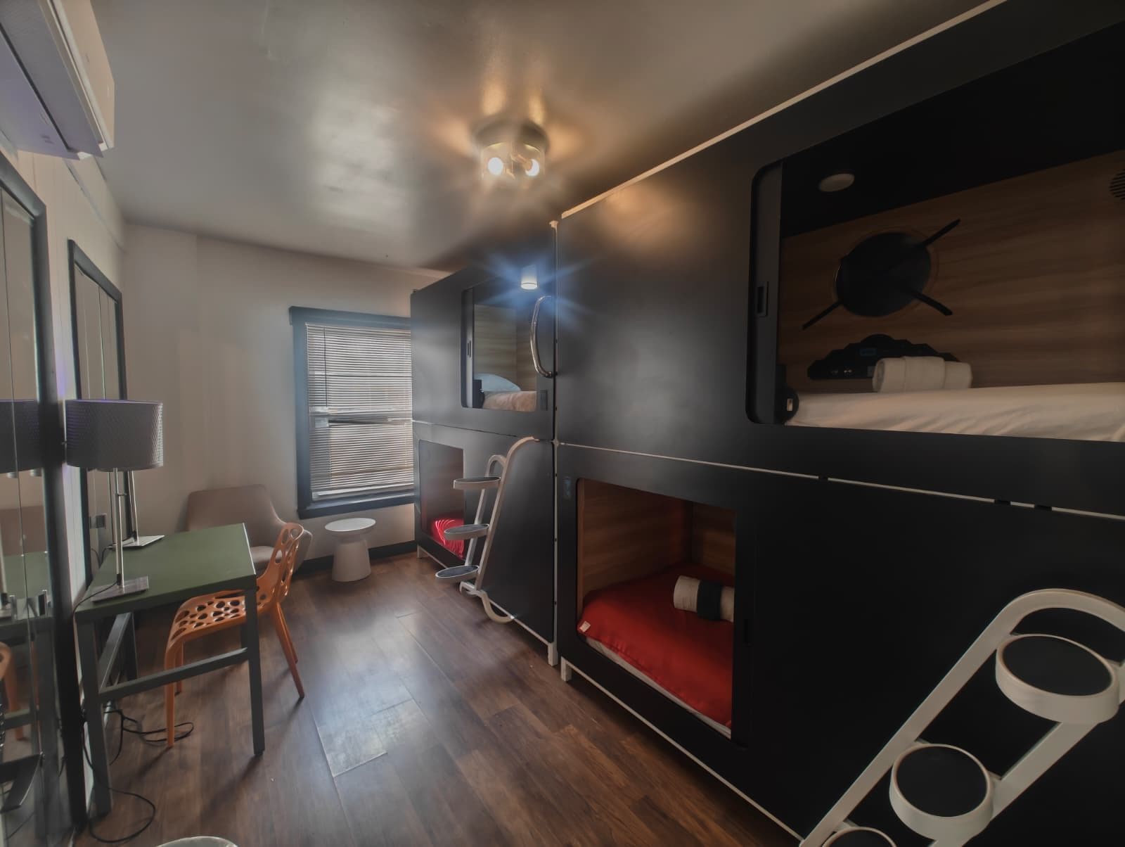 Quarto compacto com beliche, escrivaninha, cadeira e janela com persianas.