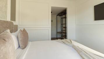 Quarto de hotel com cama, almofadas, guarda-roupa e televisão na parede.