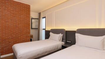Quarto de hotel com duas camas de solteiro, parede de tijolos, janela com cortinas e painel de controle fixado na parede.