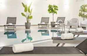 Uma área à beira da piscina com espreguiçadeiras, piscina e plantas em vasos.
