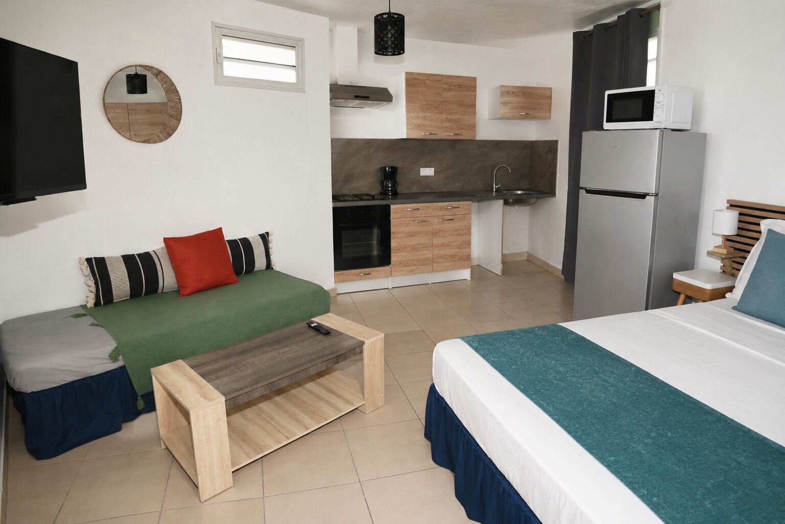 Quarto de hotel compacto com cama, um pequeno sofá, cozinha compacta e televisão.