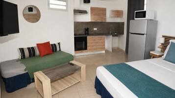 Quarto de hotel compacto com cama, um pequeno sofá, cozinha compacta e televisão.