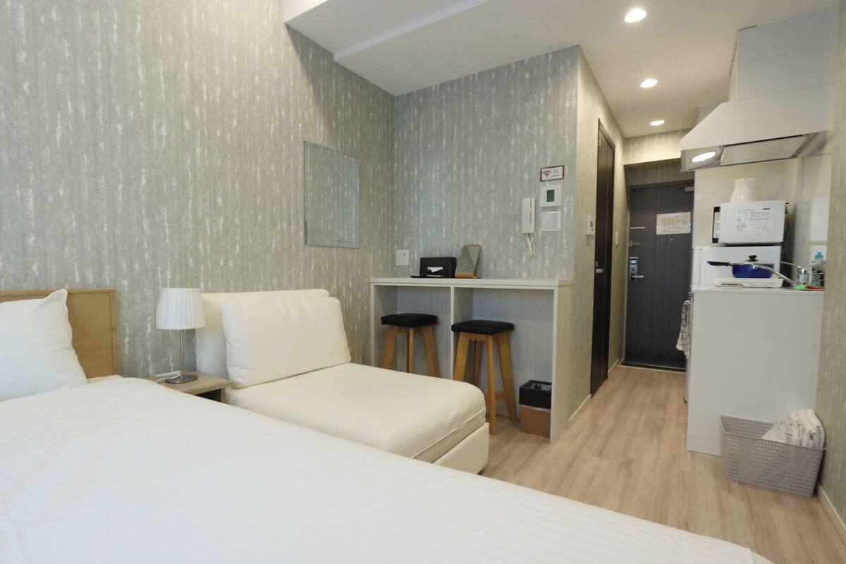 Quarto de hotel com duas camas, uma escrivaninha com cadeira, um banquinho pequeno, micro-ondas e frigorífico.
