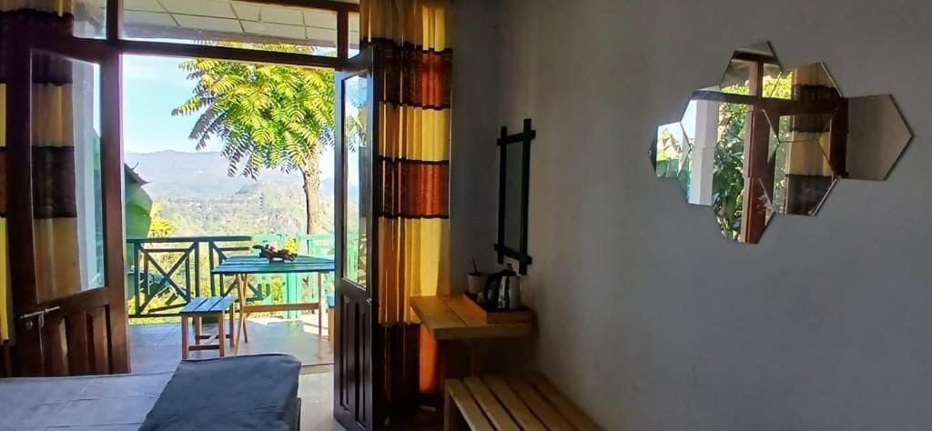Um quarto com um banco de madeira, uma mesa pequena e vista para o verde lá fora.
