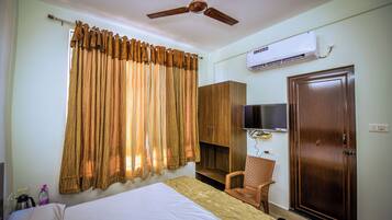 Quarto de hotel com cama, guarda-roupa de madeira, televisão e ar condicionado.