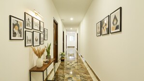 Um corredor com obras de arte emolduradas nas paredes, uma mesa consola de madeira com objetos decorativos e um chão estampado.