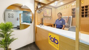 Bancada de recepção em hotel com acabamento em madeira, um espelho e uma placa com a inscrição 'fab hotels'.