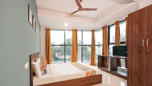 Quarto com cama, ventilador de teto, televisão e janelas amplas com cortinas.