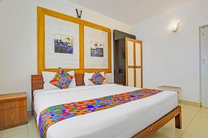 Quarto bem organizado com uma cama grande, cabeceira de madeira, duas pinturas penduradas na parede, um guarda-roupa e uma mesa de cabeceira.