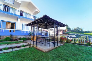 Um gazebo com teto, rodeado por um jardim com grama e plantas.