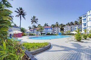 Área de piscina em resort com piscina azul cristalina, espreguiçadeiras e palmeiras.