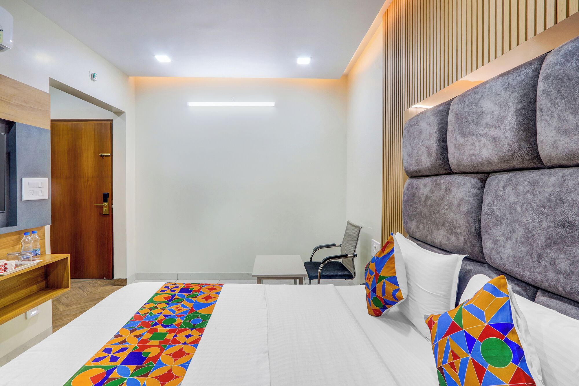 Quarto de hotel com cama, escrivaninha, cadeira e televisão.