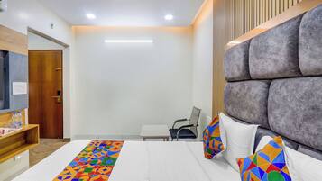Quarto de hotel com cama, escrivaninha, cadeira e televisão.