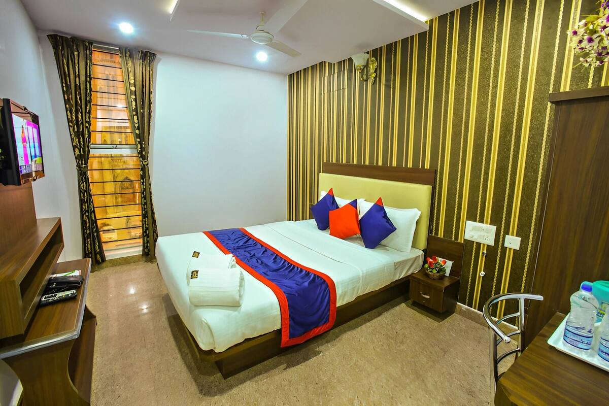 Quarto de hotel bem arrumado, com cama, mesa de cabeceira e secretária com cadeira.
