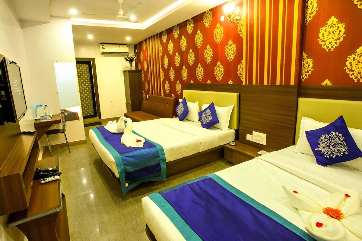 Quarto de hotel com duas camas, uma escrivaninha, um espelho e um guarda-roupa.