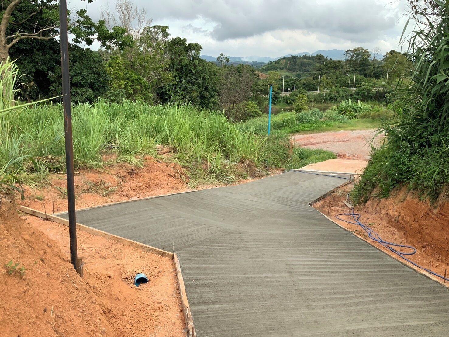 Uma trilha de concreto serpenteia por uma paisagem natural com árvores e colinas ao fundo.