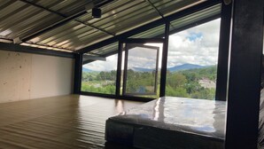 Quarto espaçoso com uma grande janela que oferece vista para montanhas e vegetação.