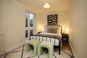 Quarto com cama, luminárias de cabeceira, janela e radiador.