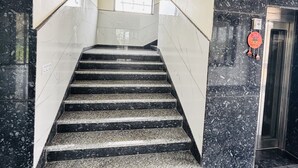 Uma escadaria com paredes de mármore preto e branco, corrimão e uma pequena janela no topo.