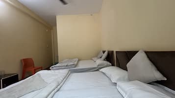 Quarto de hotel com uma cama de solteiro, ventoinha no teto e uma cadeira vermelha.
