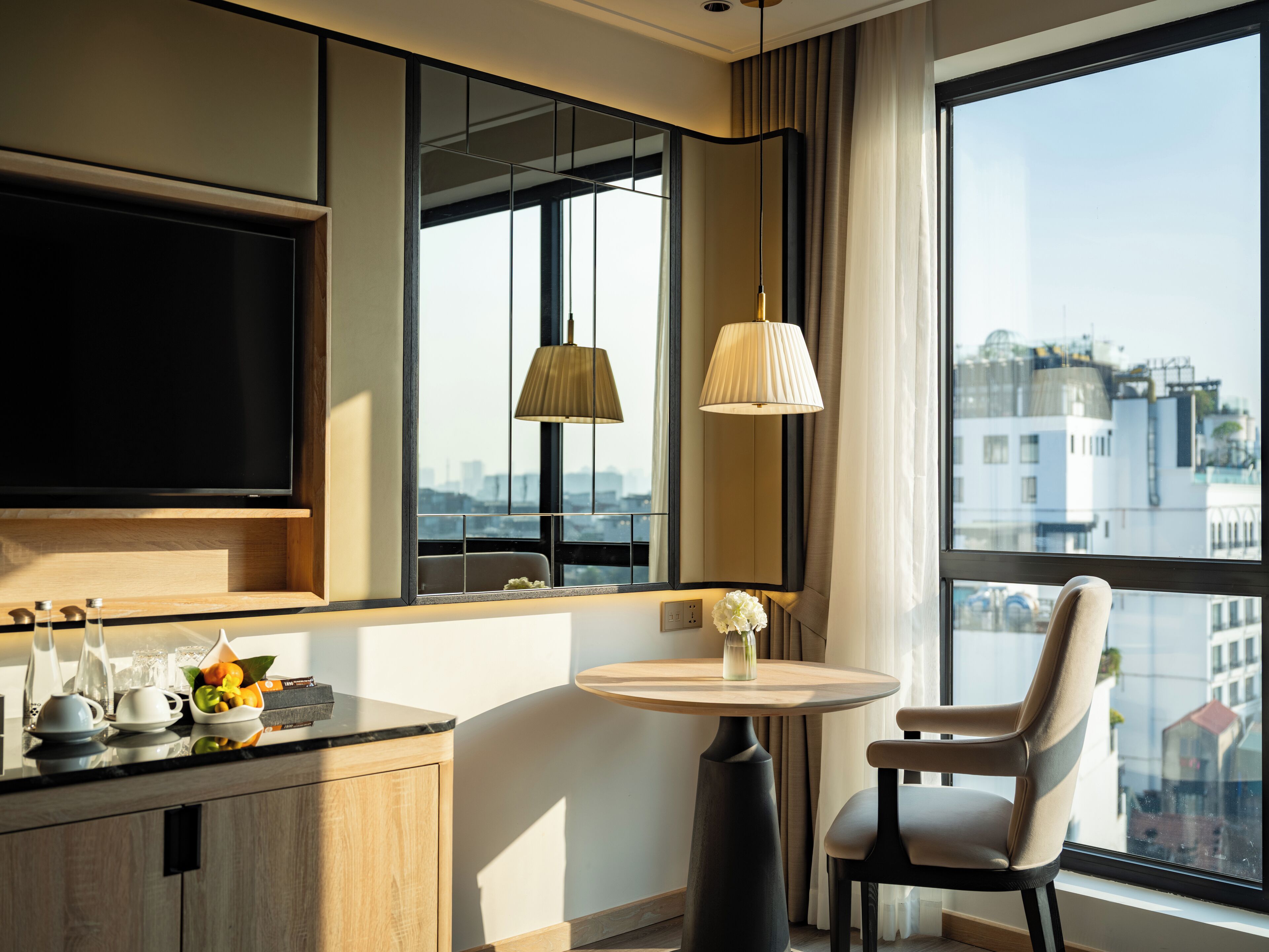 Quarto de hotel moderno com uma janela grande, televisão de tela plana, mesa de jantar redonda e uma cadeira.