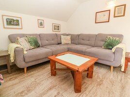 Uma sala de estar com um sofá cinzento, uma mesa de centro de madeira e quadros nas paredes.