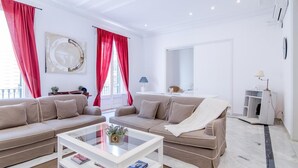 Uma sala de estar moderna com um sofá seccional bege, uma mesa de centro de vidro e cortinas vermelhas.
