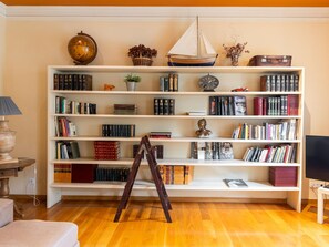 Quarto com uma grande estante cheia de livros, um globo, um modelo de navio e uma escada.