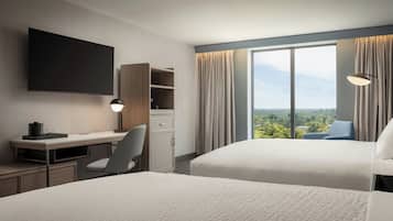 Quarto de hotel com duas camas, uma escrivaninha com cadeira, televisão e uma janela grande com cortinas.