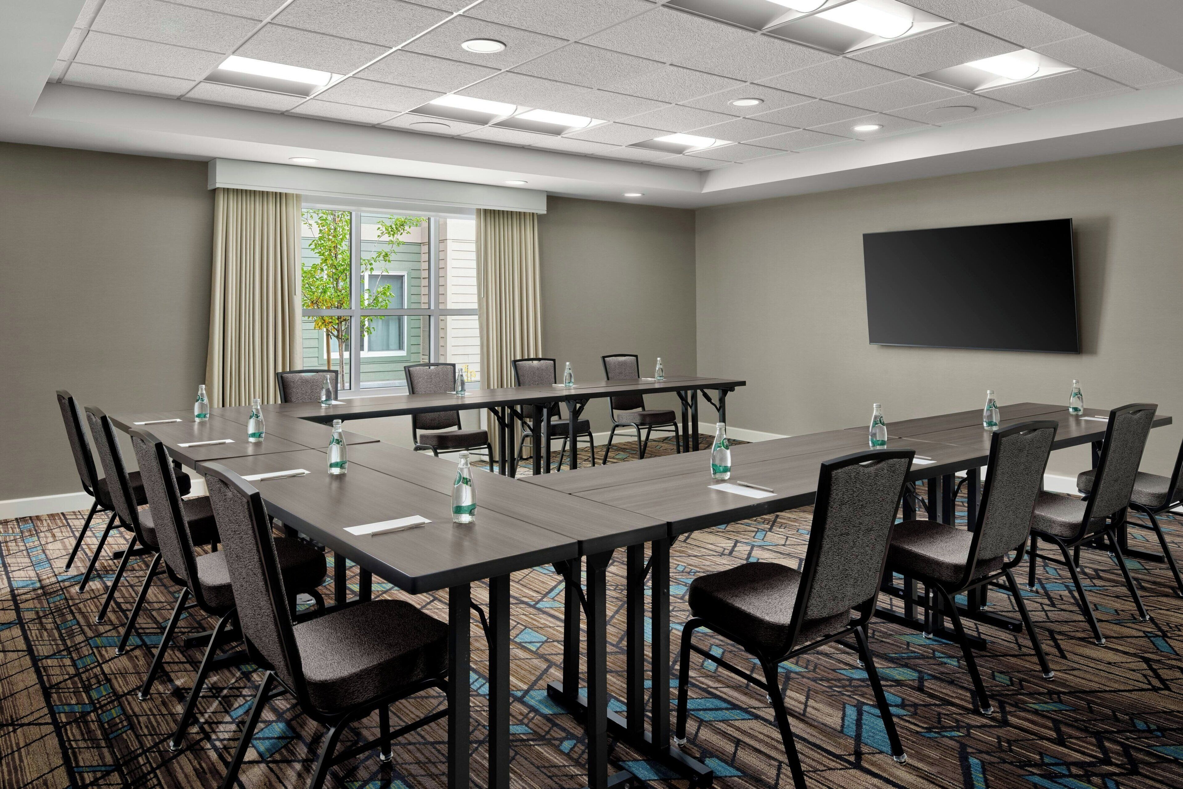 Sala de conferência com uma mesa comprida, cadeiras, tela de projetor e janela com cortinas.