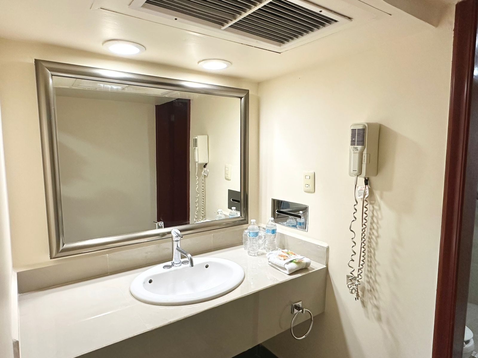 Casa de banho de hotel com um espelho grande, lavatório e secador de cabelo fixado na parede.