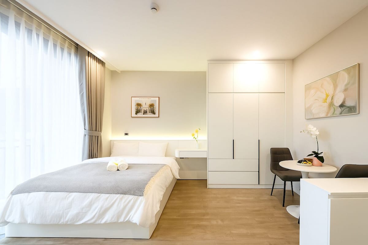Quarto de hotel moderno com cama grande, escrivaninha, cadeira e guarda-roupa.