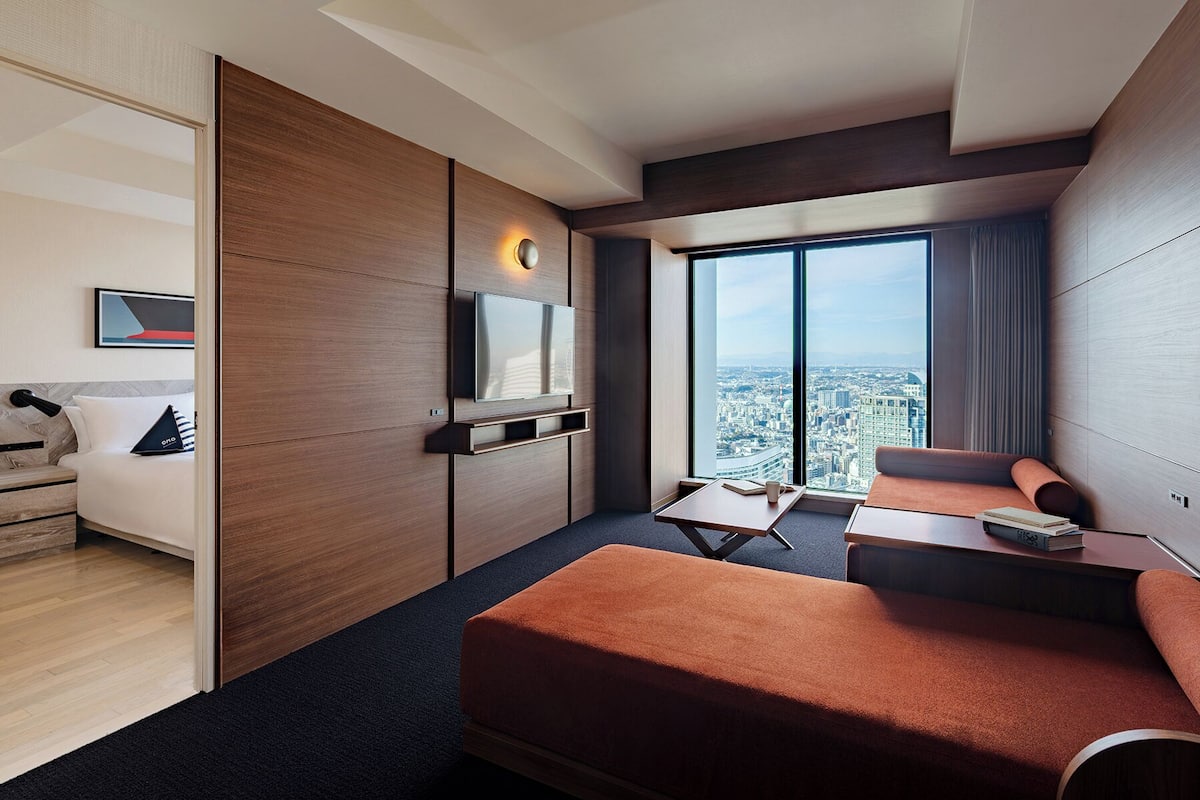 Quarto de hotel moderno com uma cama grande, uma escrivaninha, um sofá e uma televisão.