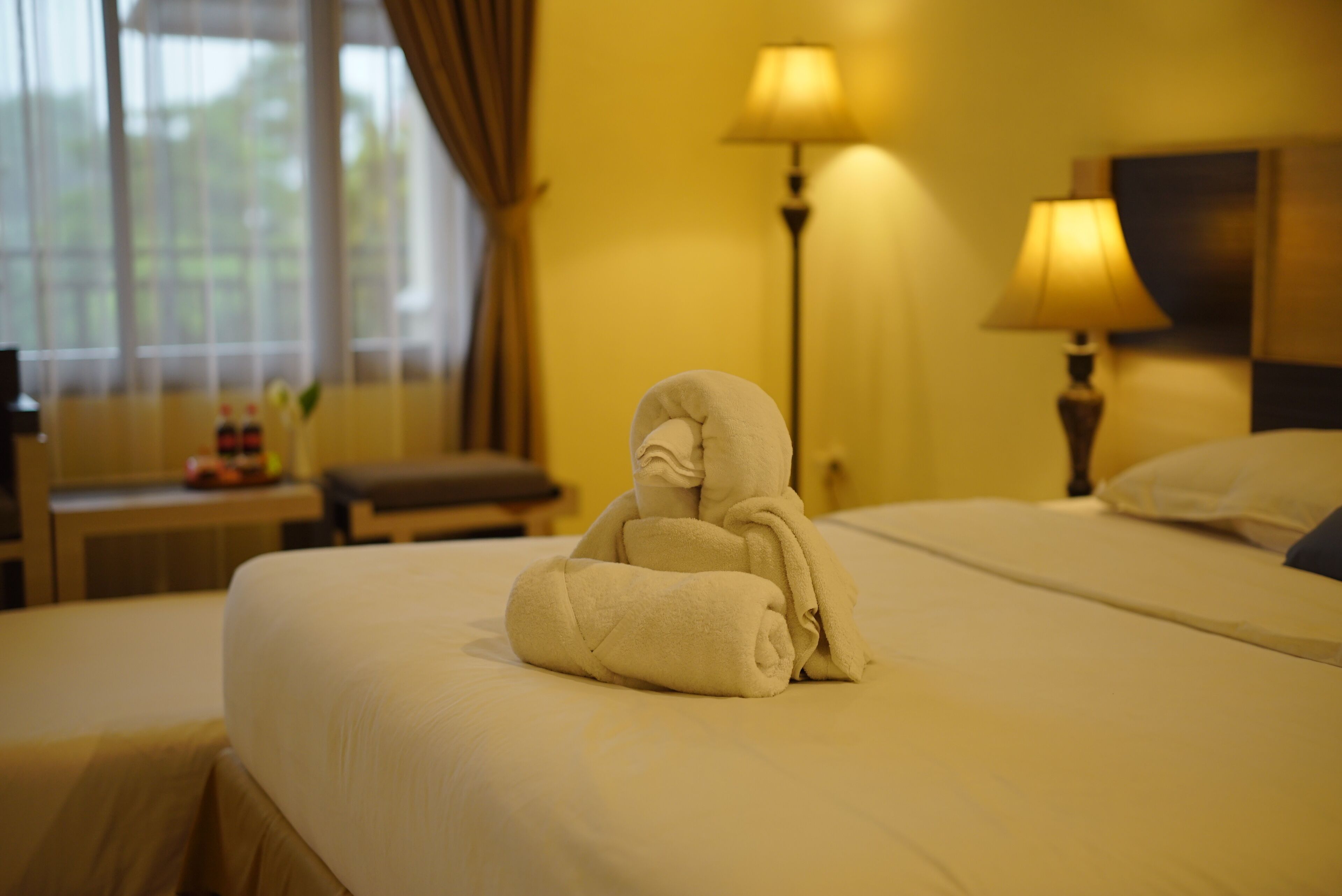 Quarto de hotel com duas camas, uma mesa de cabeceira com abajur e uma janela com cortinas.