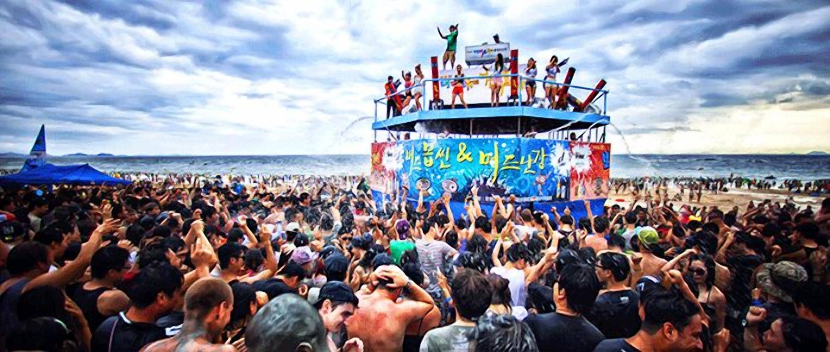 Uma praia cheia com um grande grupo de pessoas reunido em volta de um palco.