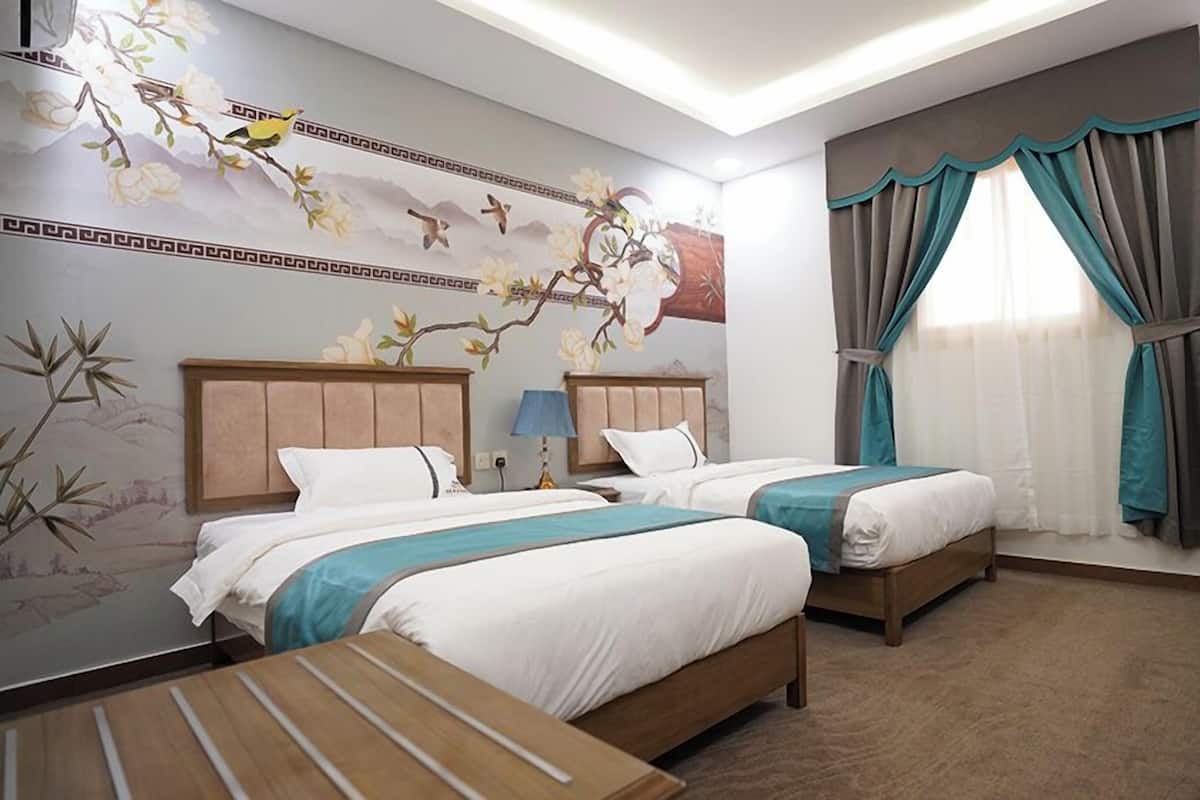 Quarto de hotel com duas camas, cabeceira de madeira, janela grande com cortinas e um mural na parede.