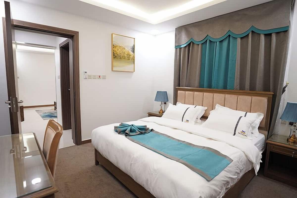 Quarto de hotel com cama, mesas de cabeceira, escrivaninha e uma cadeira.