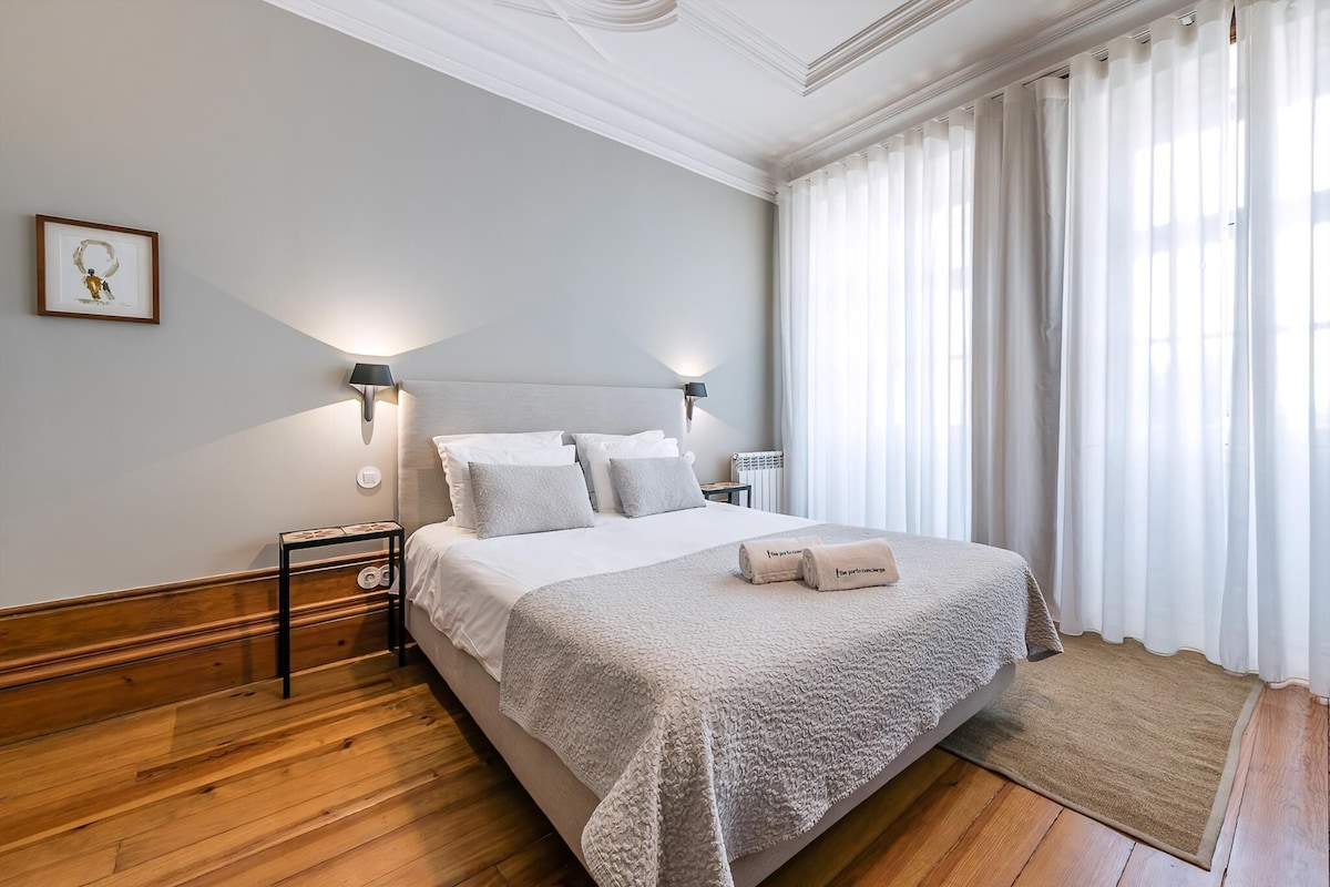 Quarto bem arrumado com uma cama grande, duas luminárias de cabeceira, um quadro na parede e piso de madeira.