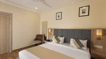 Quarto de hotel com uma cama grande, uma escrivaninha, uma cadeira e um ventilador de teto.